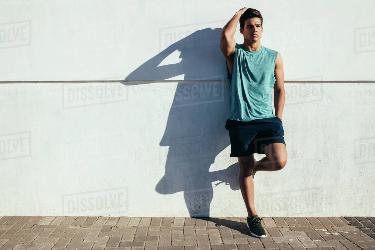 Full length shot of fit young man standing against a wall outdoors ...
