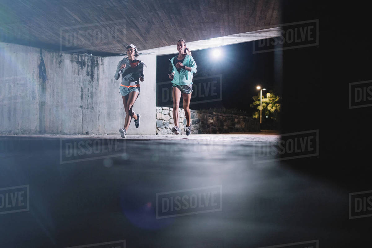 Two young female runners running together at night in city. Young women ...