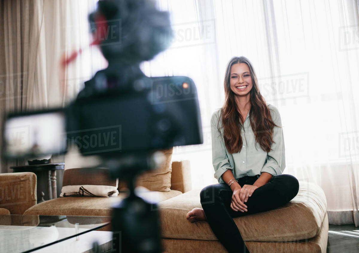 Young woman recording video on camera mounted on a tripod for her vlog ...