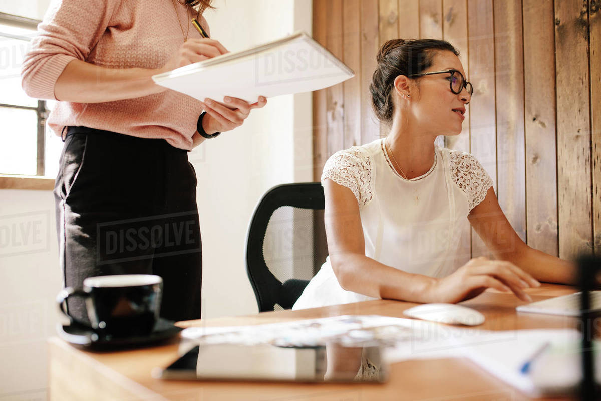 Business woman working at her desk with female colleague standing by ...