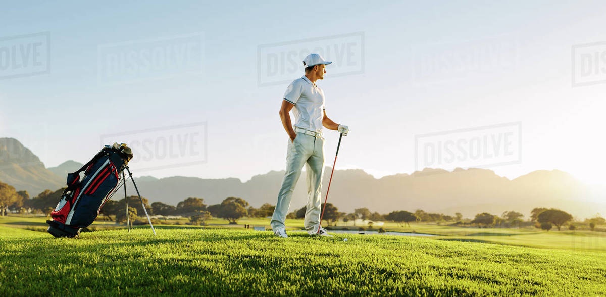 Full length of young man standing on golf course at sunset and looking ...