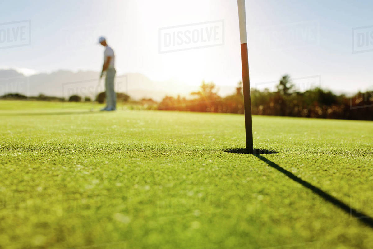 Golf hole and flag in the green field with golfer in background ...