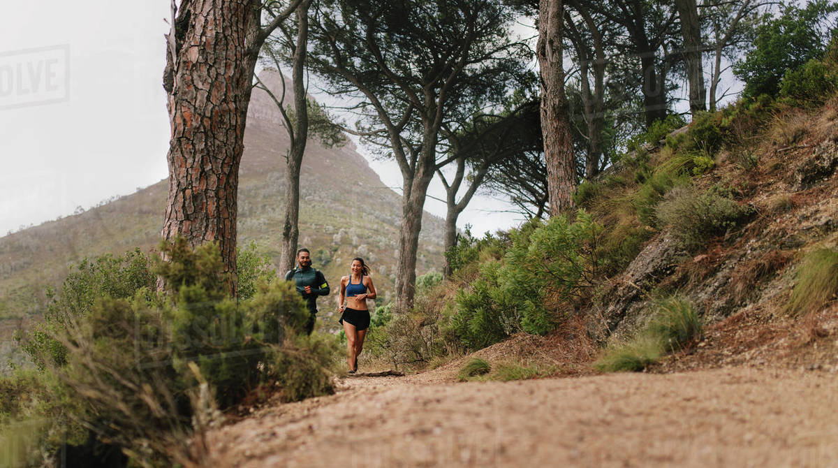 Outdoor shot of young people trail running on a mountain path. Couple ...