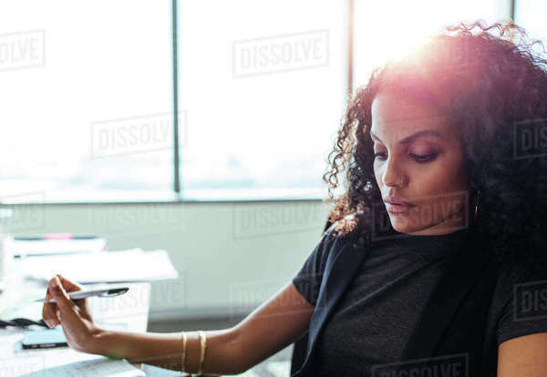 Closeup of a businesswoman sitting at her desk holding a pen. Woman ...