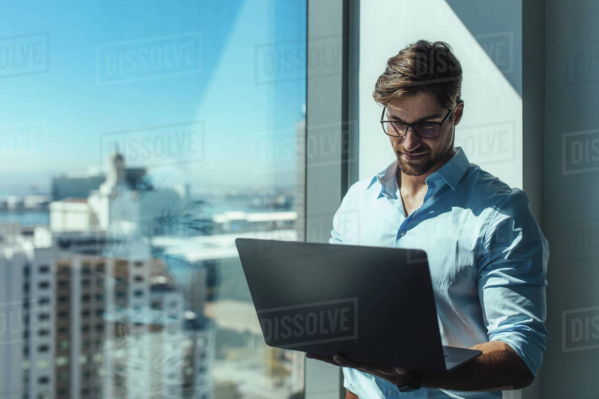 Young businessman working on a laptop computer standing in office. Man ...
