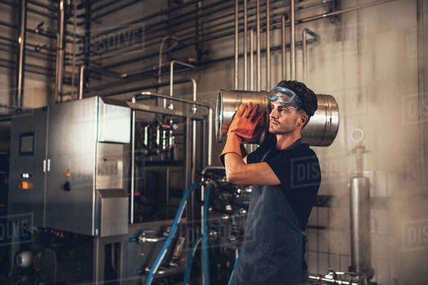 Shot of young man with metal beer barrels at brewery. Brewer carrying ...
