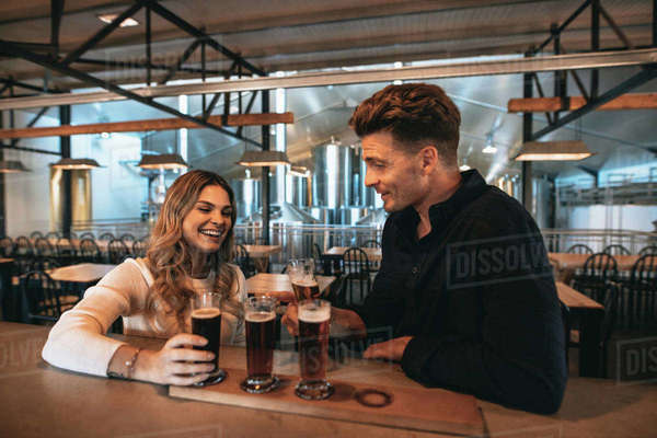 Happy young man and woman at brewery with selection of four different ...