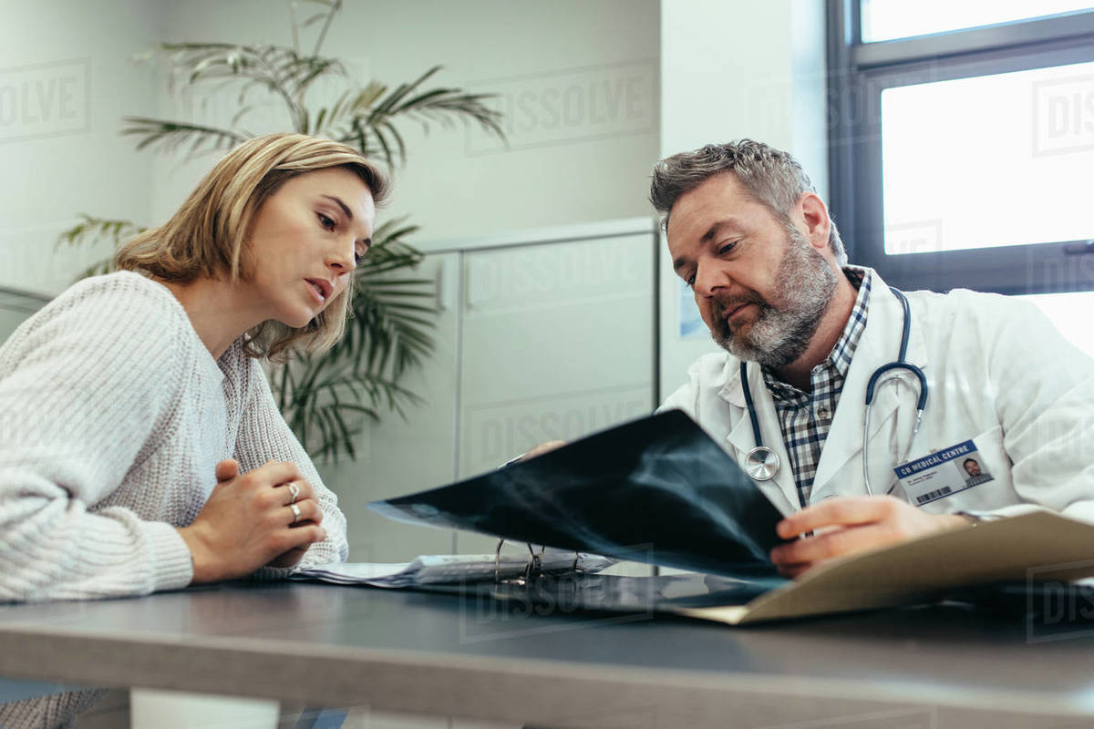 Doctor showing diagnosis of x-ray image to female sitting at office ...