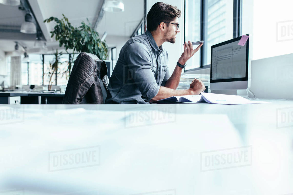 Young businessman talking on speaker phone. Young man sitting in office ...