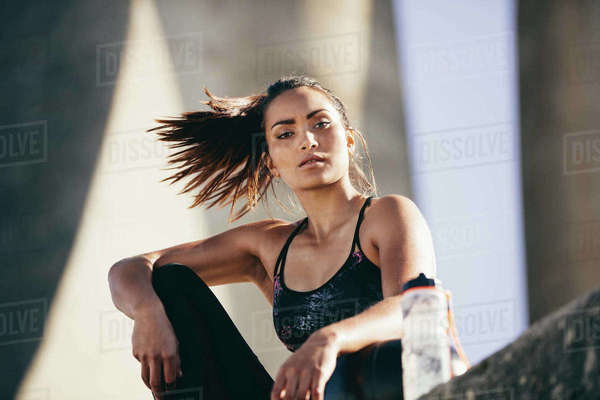 Fit young woman sitting outdoors after workout session in morning ...