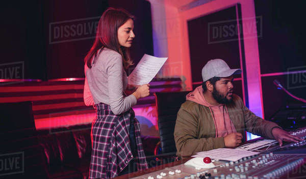 Female singer with man working on audio mixing console in recording ...