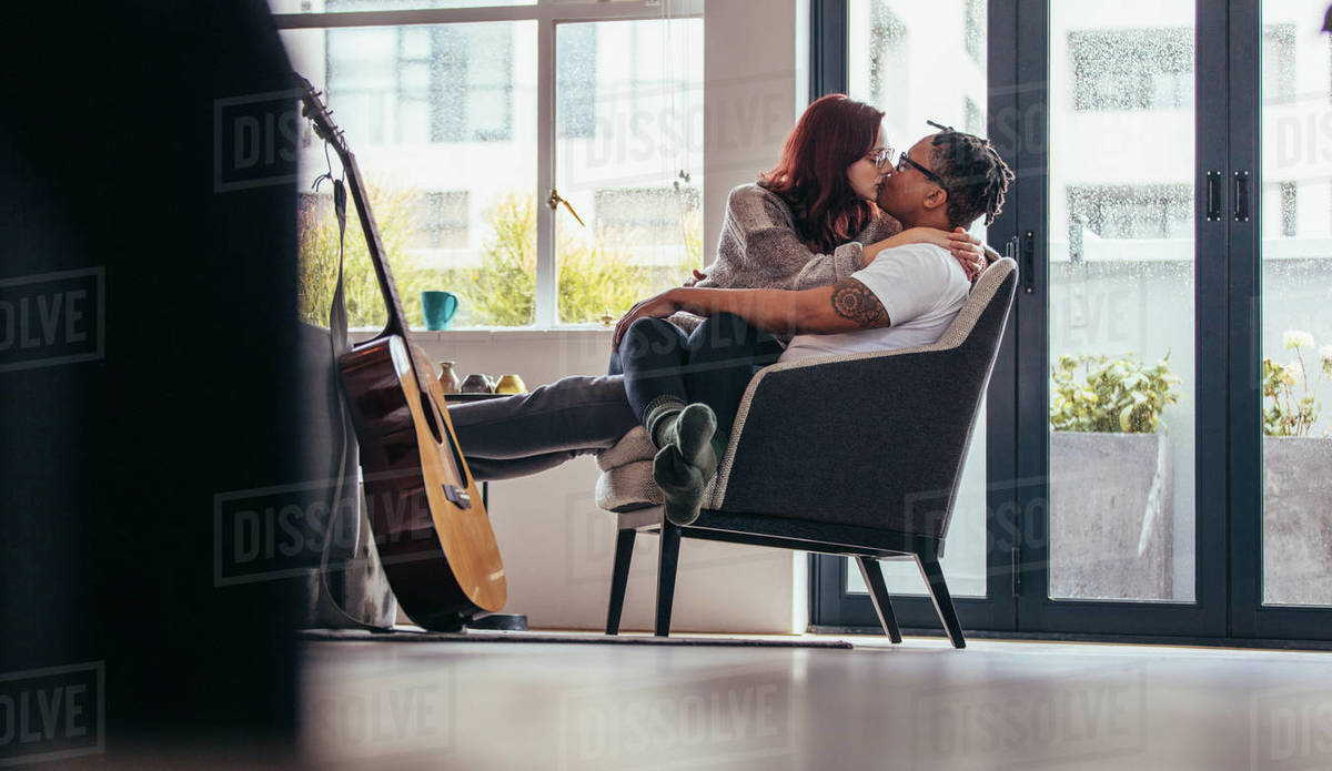 Interracial couple sitting on a armchair and kiss one another. Woman ...