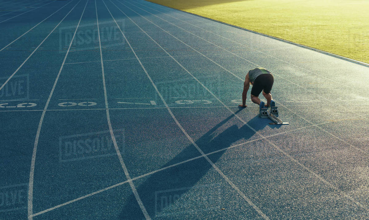 Rear view of an athlete ready to sprint on an all-weather running track ...
