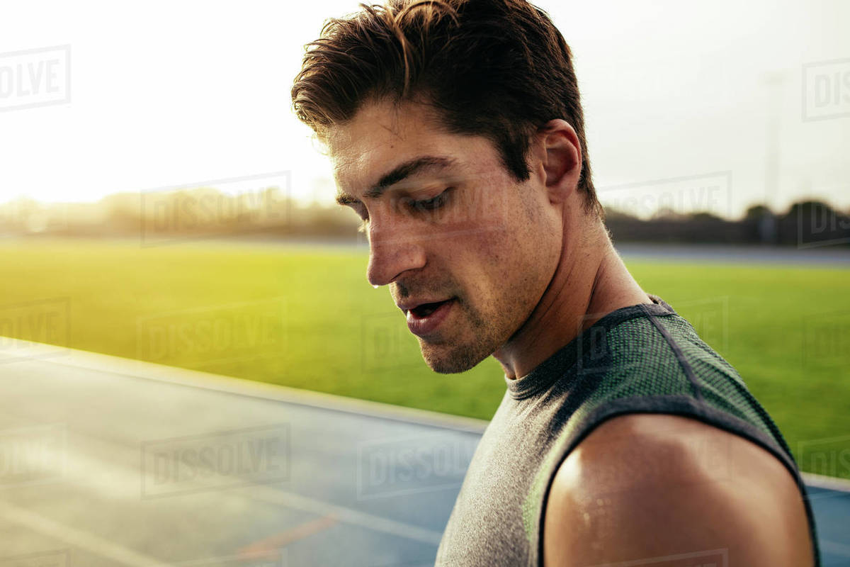 Closeup of a sprinter standing on a running track. Runner looking down ...