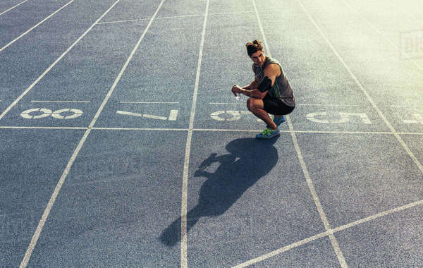 Athlete sitting on running track with a water bottle in hand. Runner ...