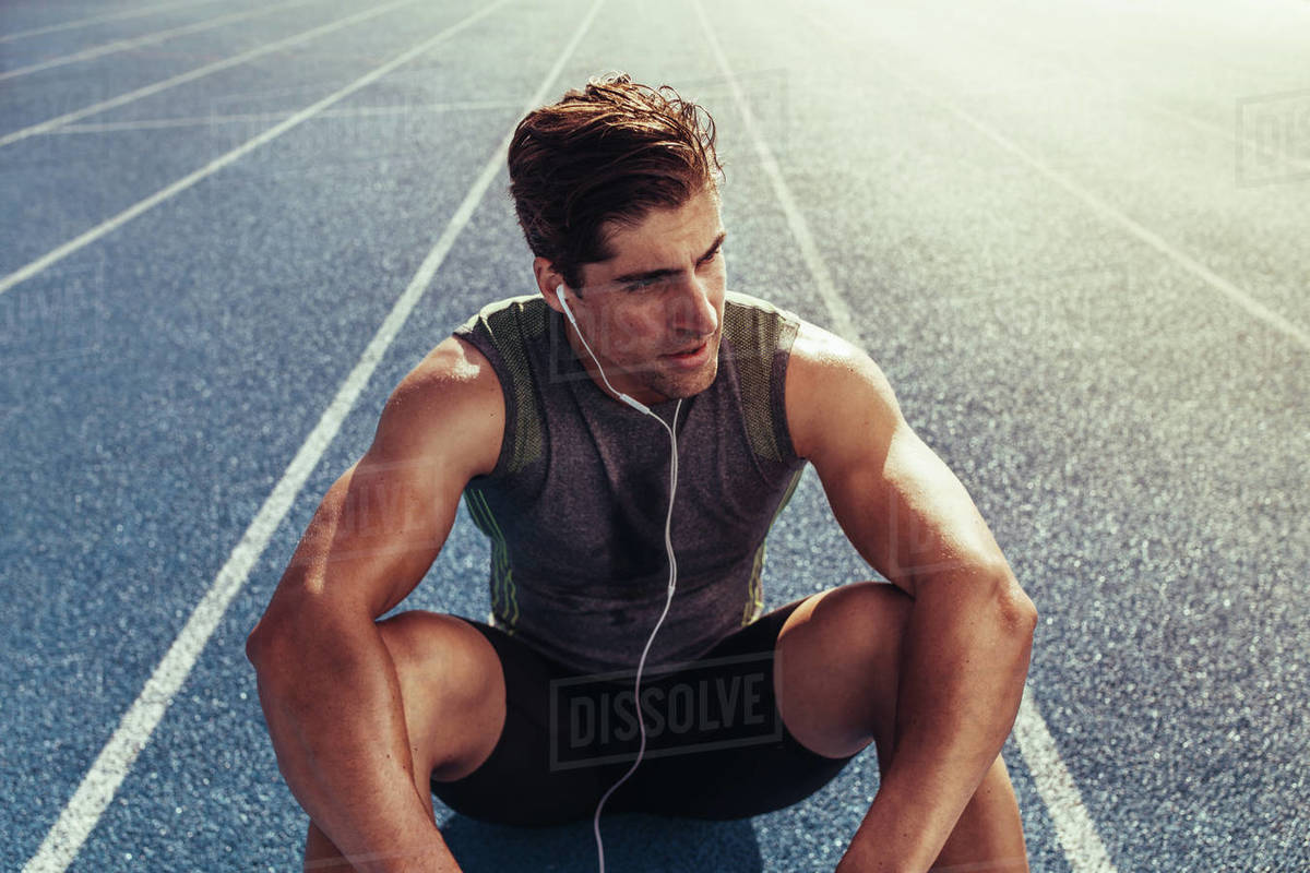 Close up of an athlete sitting on a running track listening to music ...
