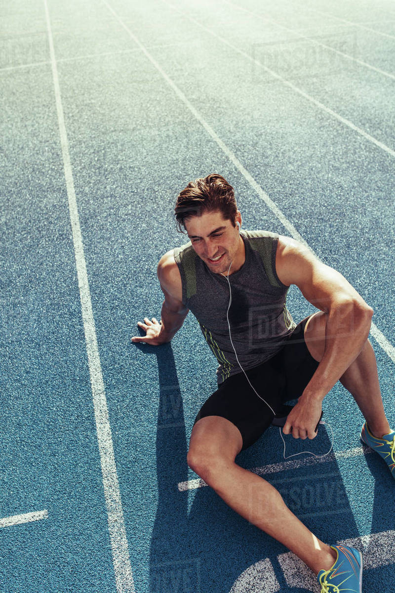 Smiling athlete sitting on a running track listening to music. Runner ...