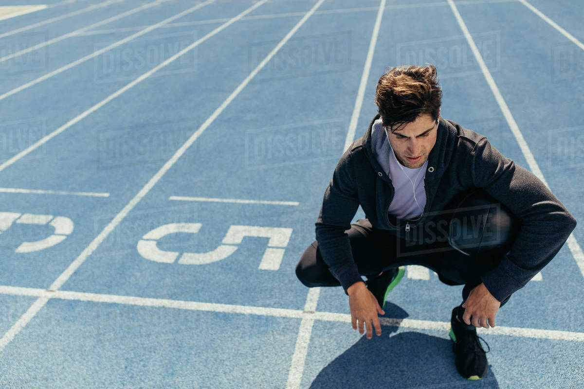Athlete sitting on a running track near the start line with a medicine ...