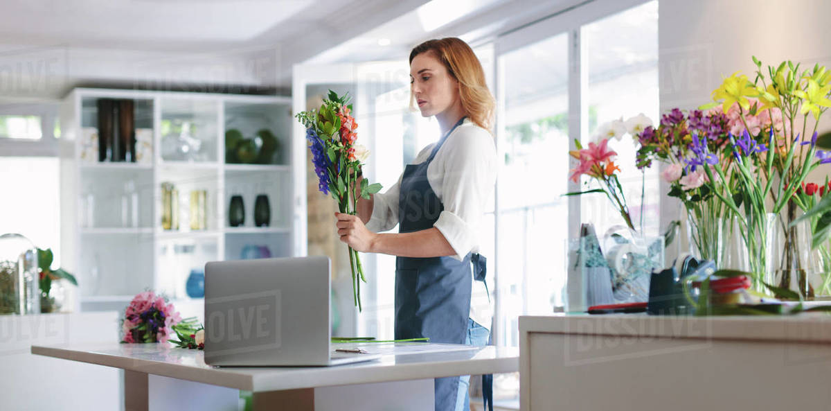 Female florist at work creating a bouquet. Woman standing at table with ...