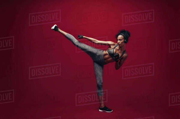 African female fighter practising high kick in studio. Full length shot ...