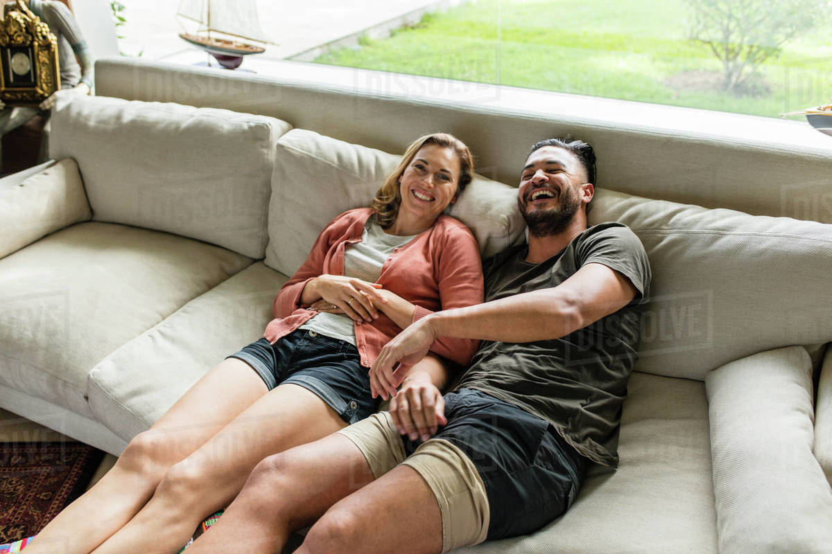 Smiling young couple relaxing on sofa in living room. Man and woman ...