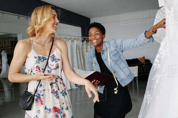 Shop assistant helps the bride in choosing bridal dress at shop of ...