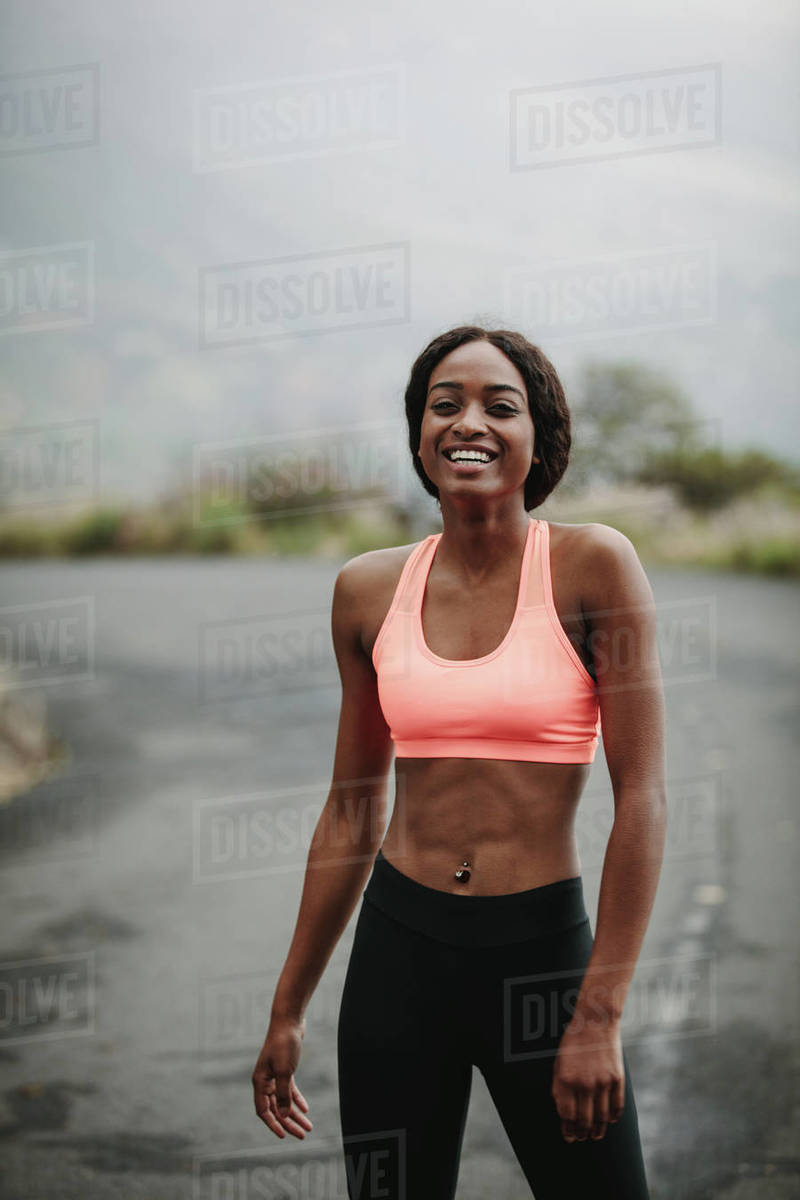 Woman athlete in running gear standing on empty road. Smiling athlete ...