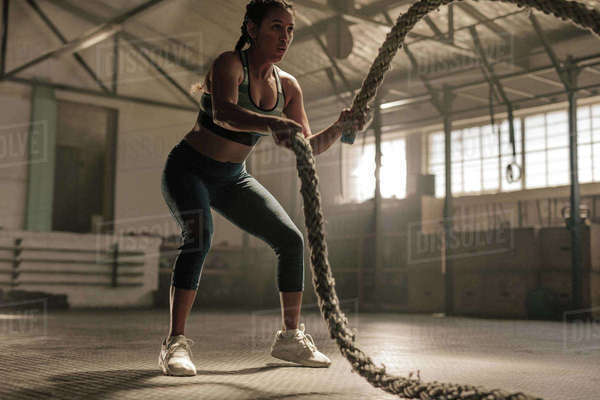 Young woman doing strength training using battle ropes at the gym ...