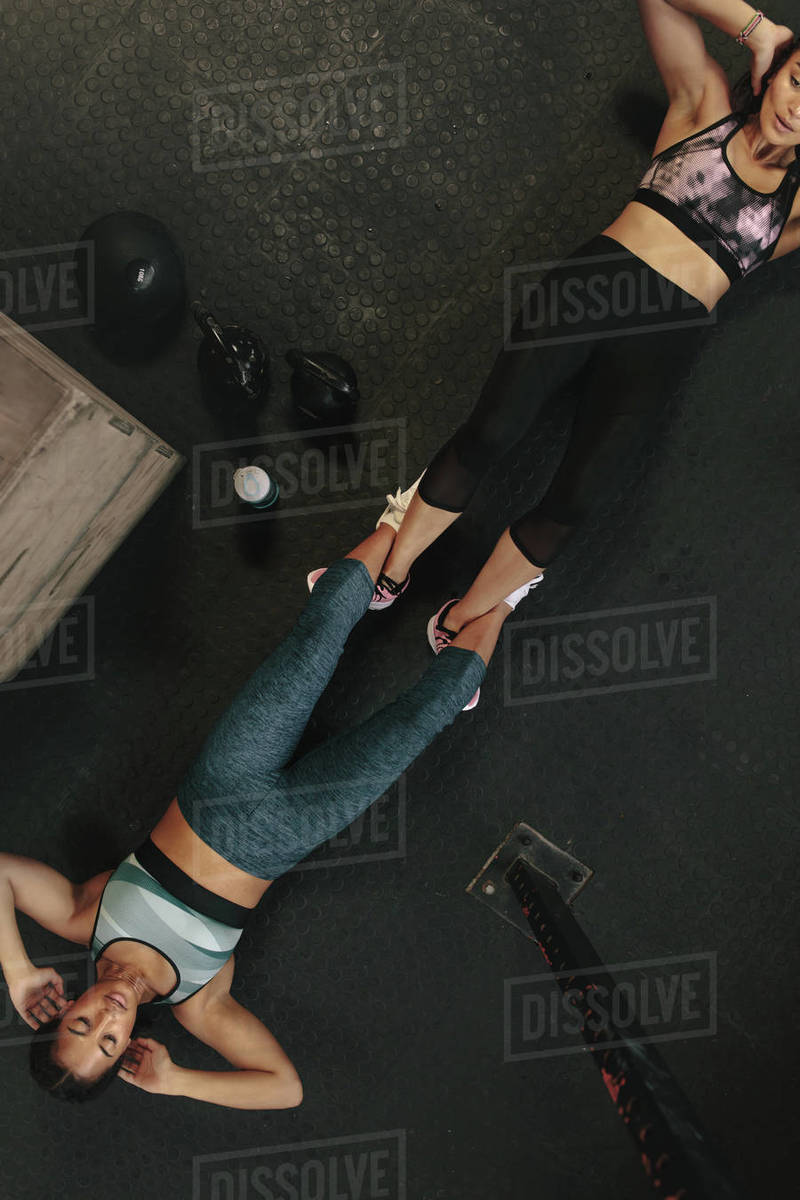Top view of two women locking their legs and doing sit-ups at gym ...