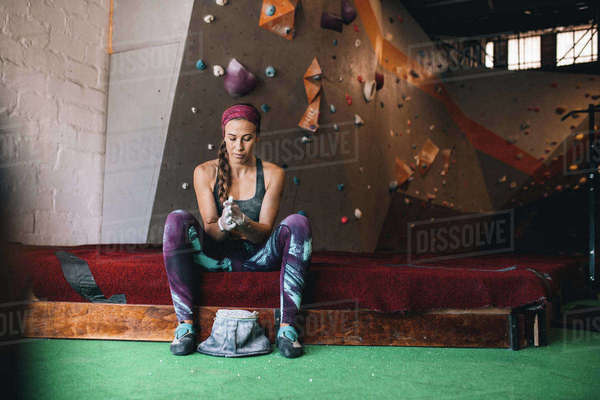 Woman at a wall climbing gym applying magnesium chalk powder on hands ...
