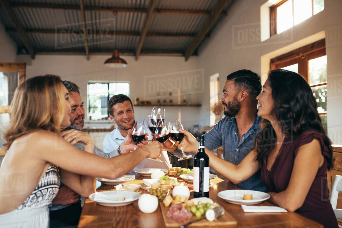 Cheerful friends toasting red wine at dinning table during dinner party ...