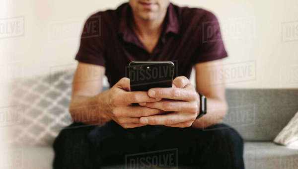 Close up of man working on mobile phone sitting on sofa. Man operating ...