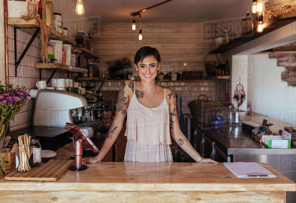 Woman standing at the billing counter of her cafe posing. Smiling ...