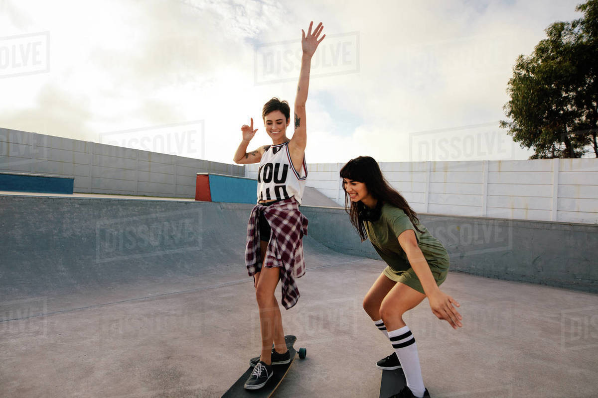Two female friends skateboarding together at skate park. Young women ...