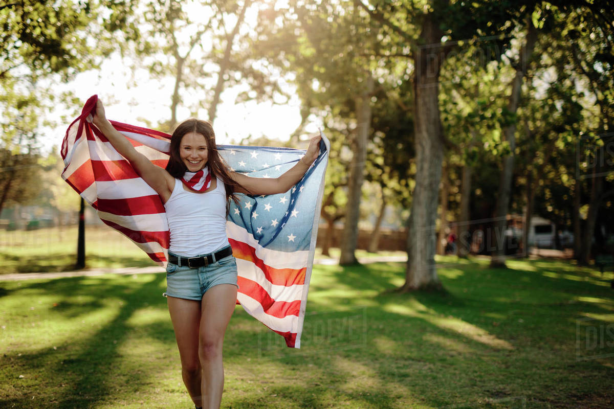 Beautiful young woman walking in the park and waving American flag ...