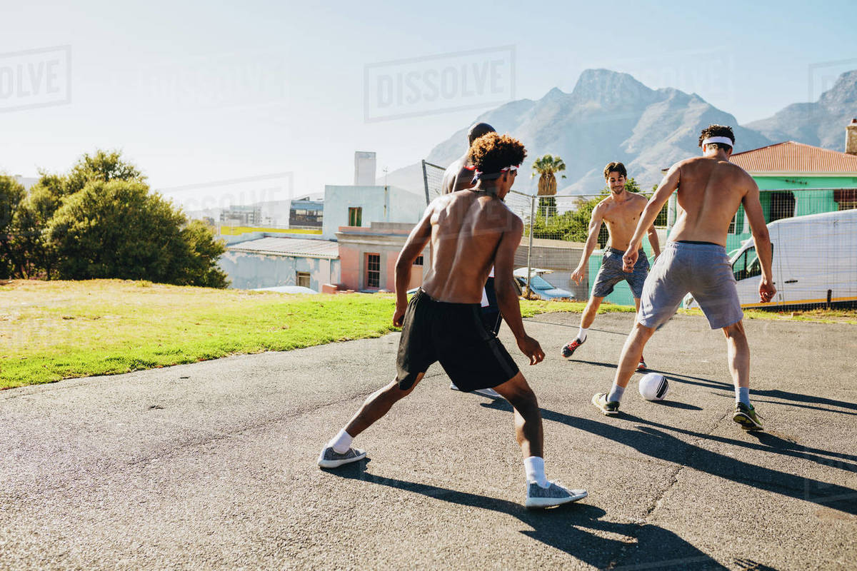 Four men playing football in play area. Men practicing football on a ...