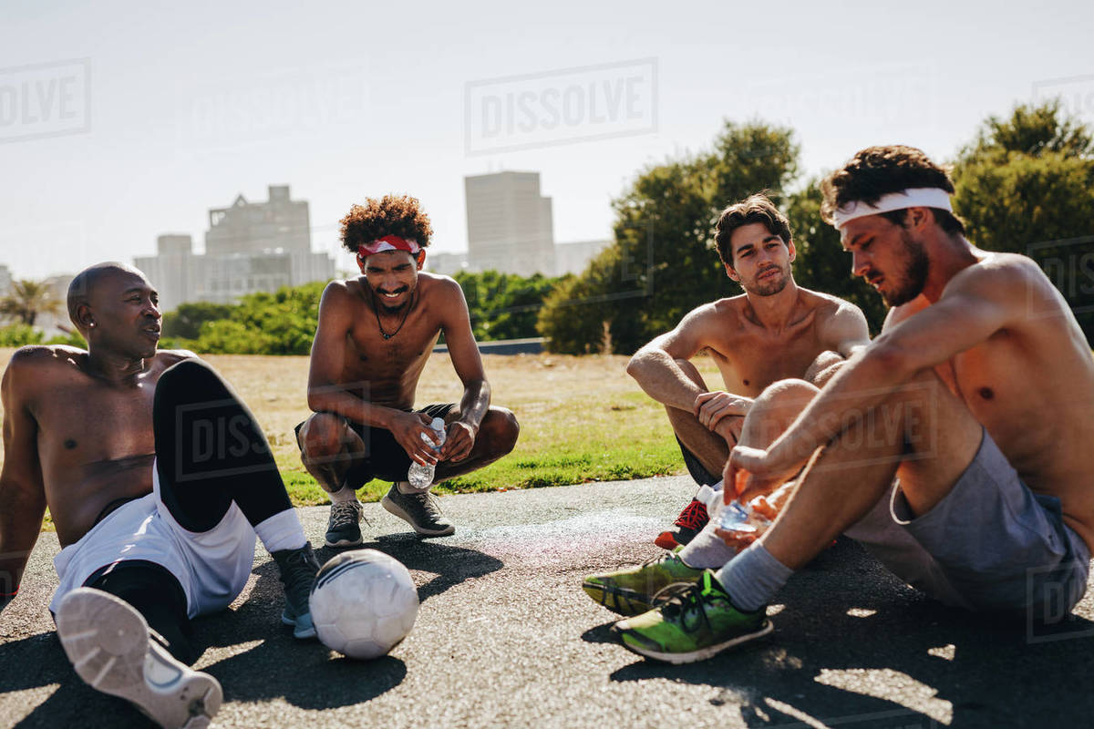 Football players sitting on ground and talking during a break. Tired ...