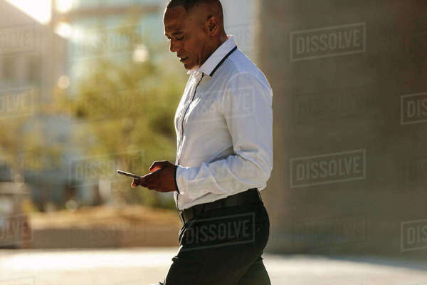 Man in formal clothes looking at his mobile phone while walking on ...