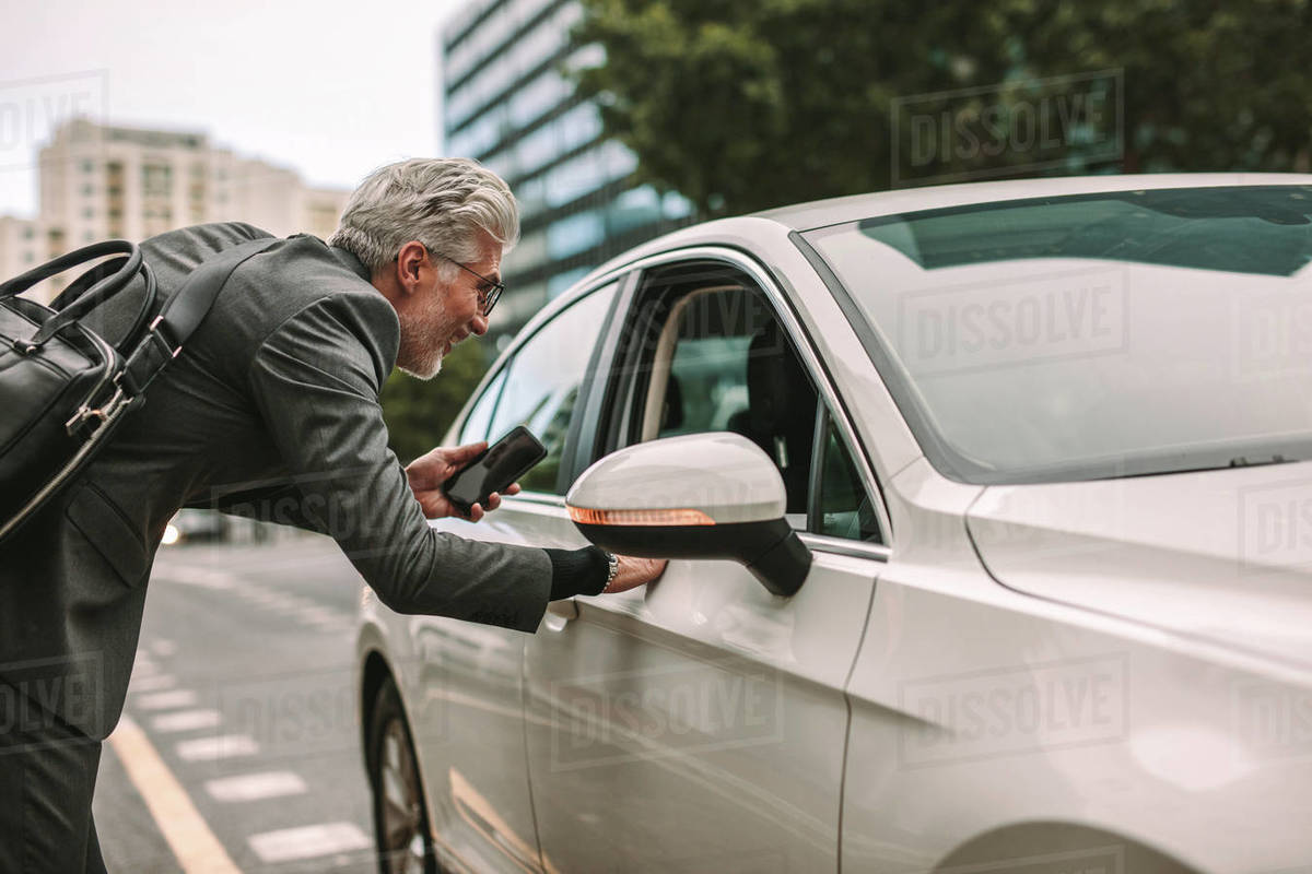 Senior man standing on road and talking to taxi driver through opened ...