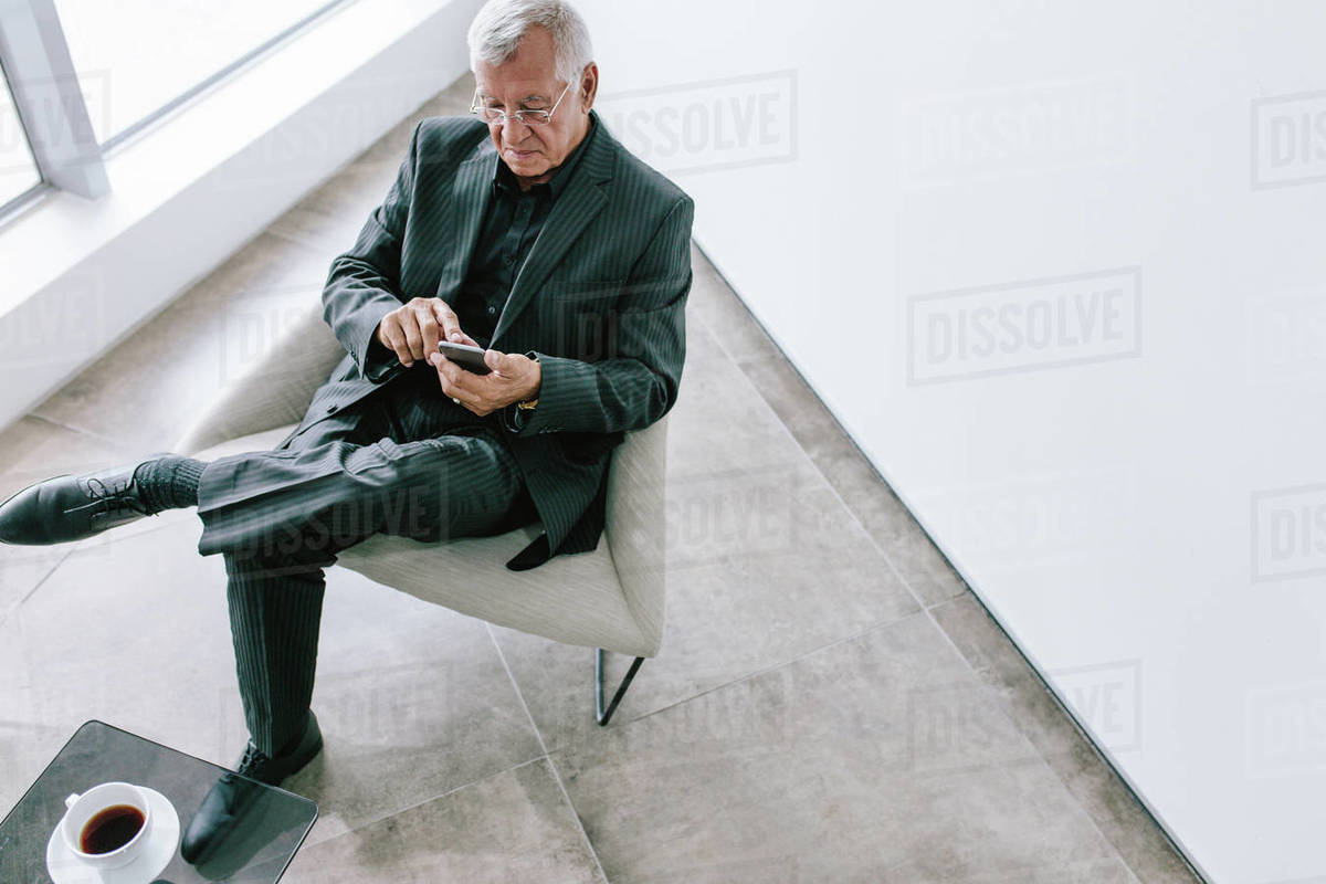 To view of old businessman using with mobile phone in office lobby ...