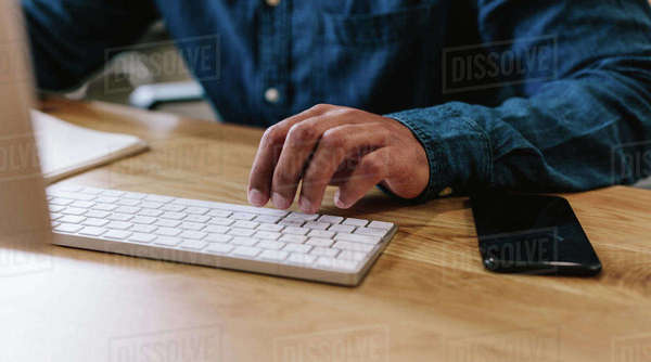 Close up of young man hands typing on computer keyboard on his desk ...