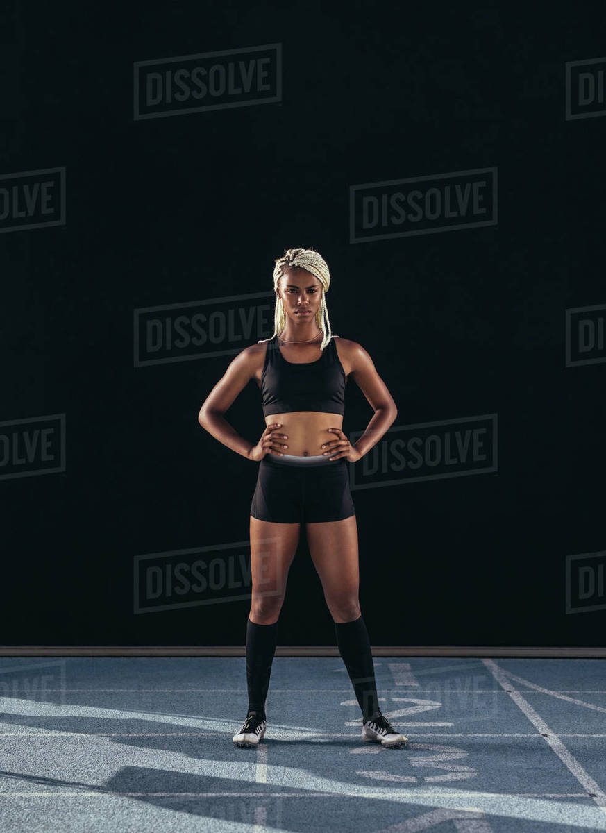 Female athlete standing at the start line on running track on a black ...