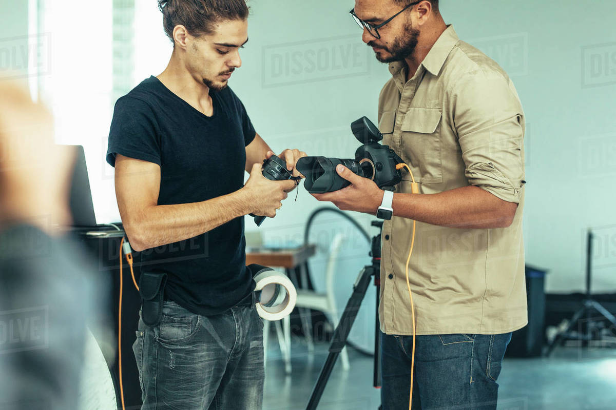 Camera assistant helping a photographer in changing lens on a DSLR ...