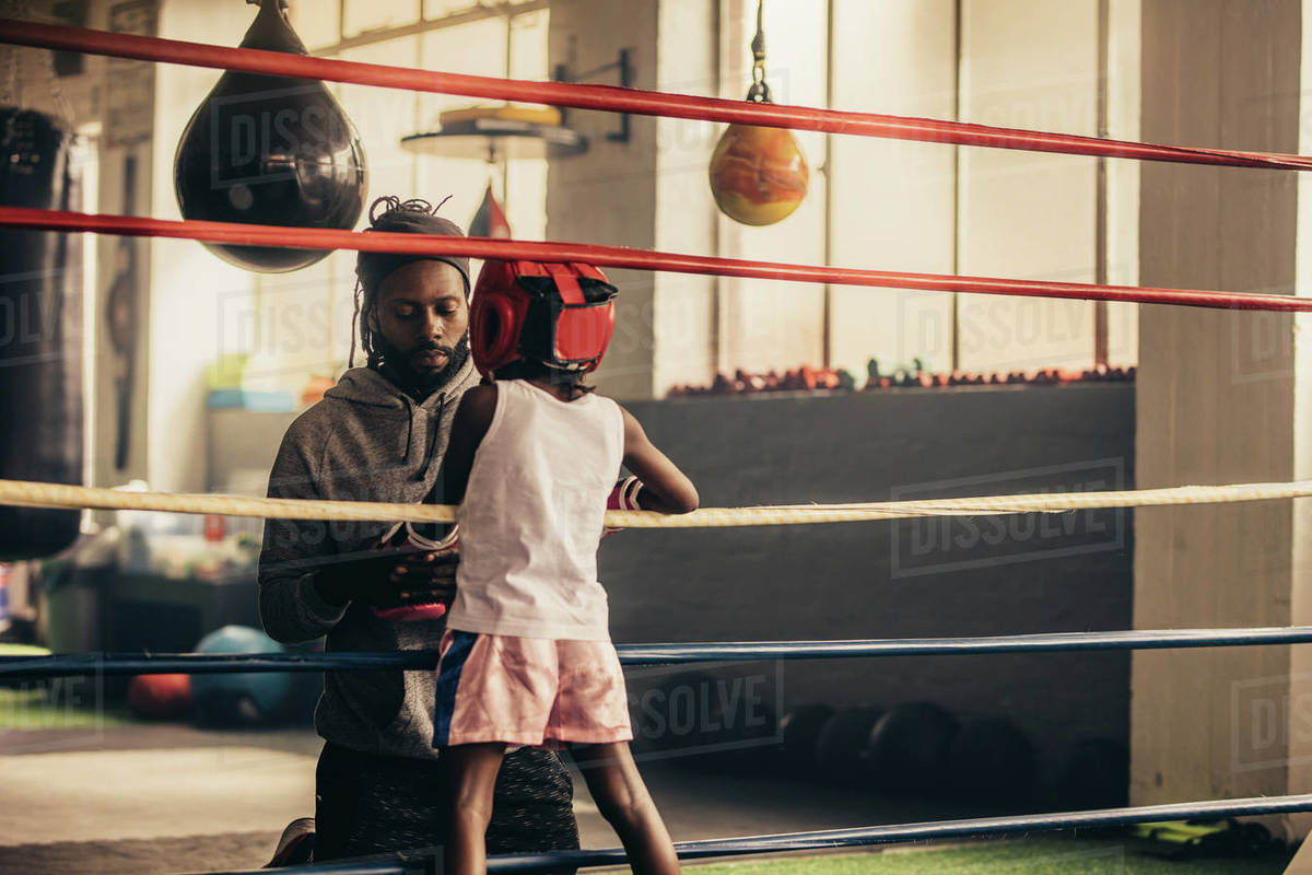 Rear view of a boxing kids talking to his coach standing inside the ...