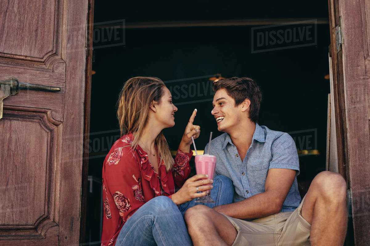 Happy couple sitting together sharing a milkshake with two straws ...