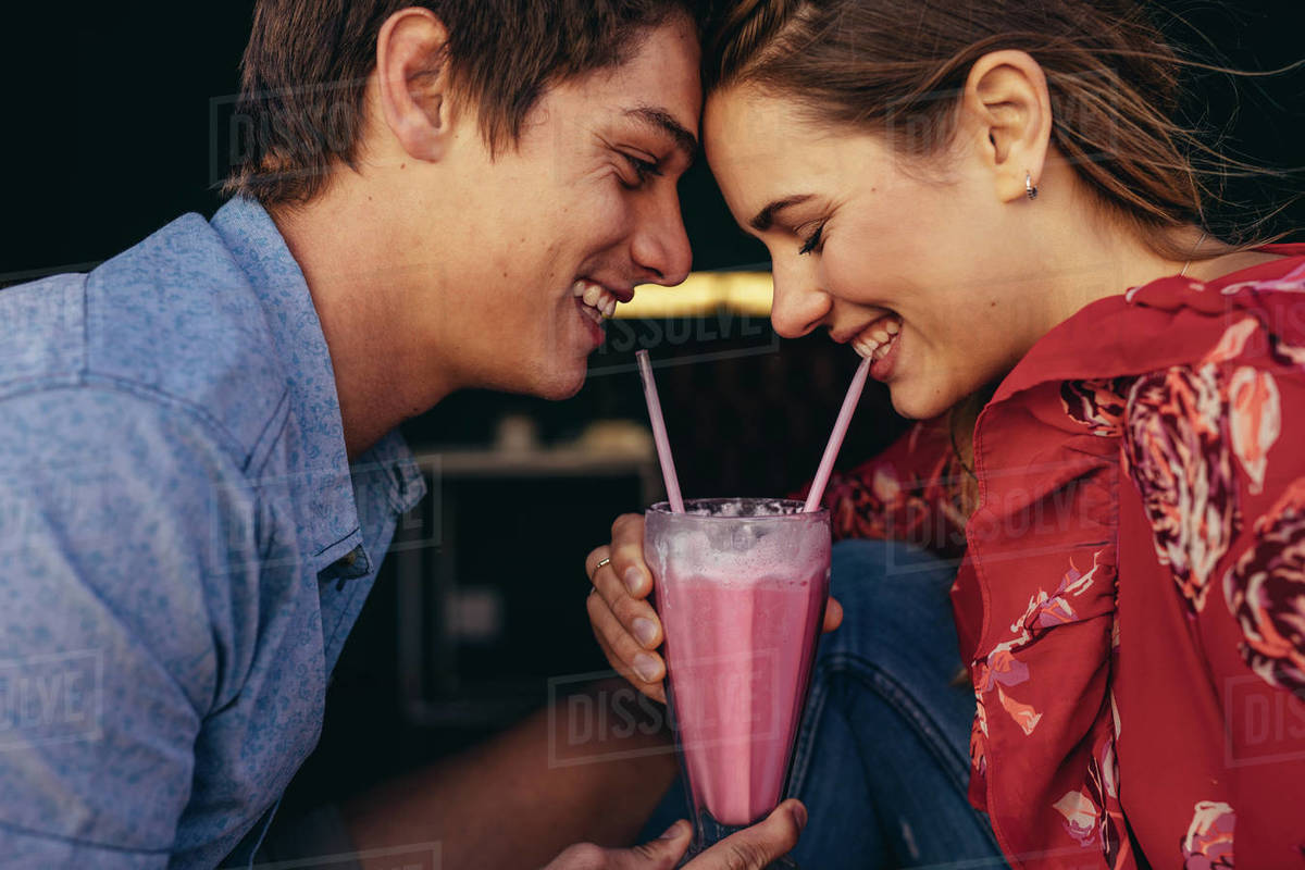 Close up of a happy couple sharing a milkshake with two straws. Smiling ...