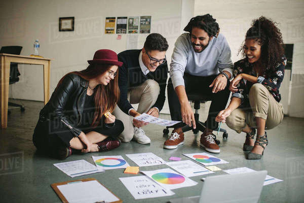 Cheerful business colleagues sitting on floor in office and discussing ...