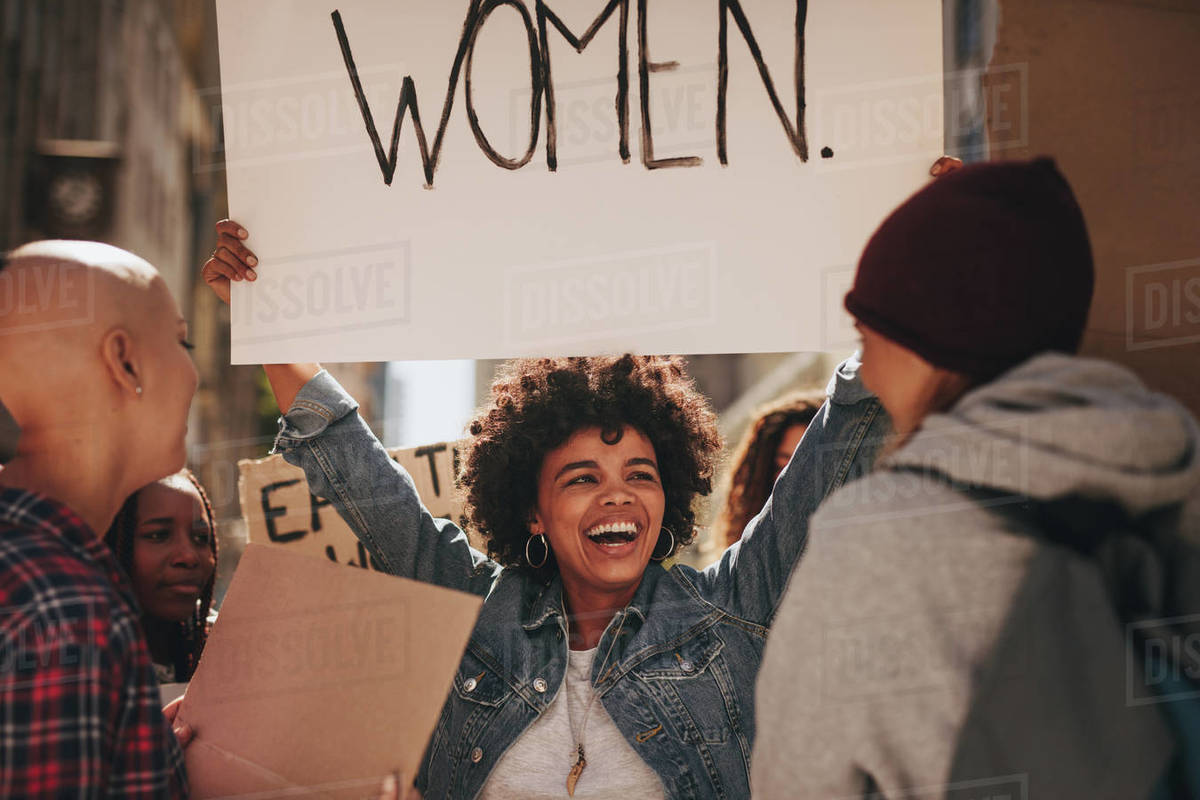 African woman holding hand written protest sign and smiling with group ...
