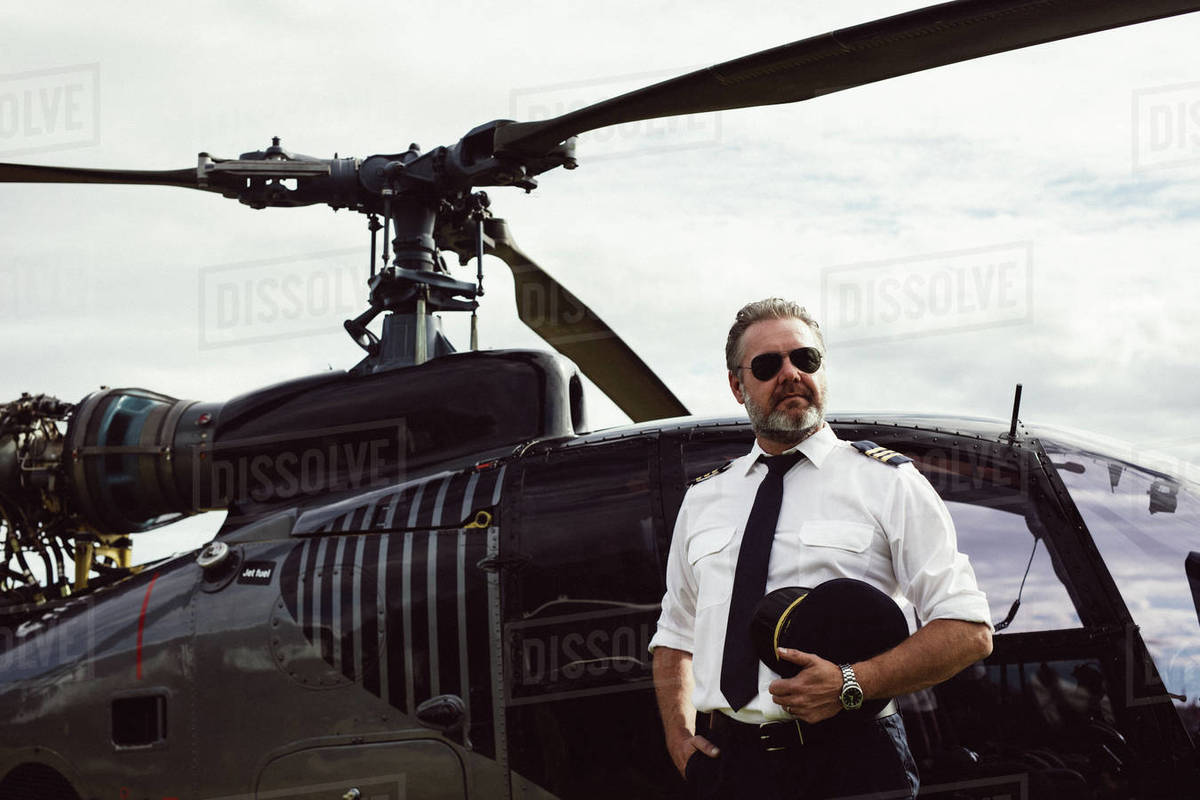 Handsome male helicopter pilot in uniform standing outdoors. Private ...