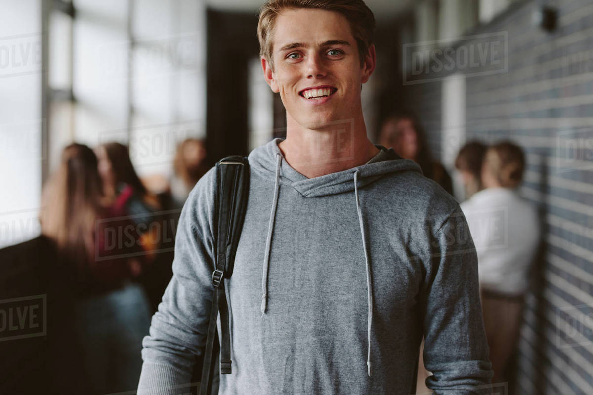 Portrait of happy young guy with bag walking in university corridor ...